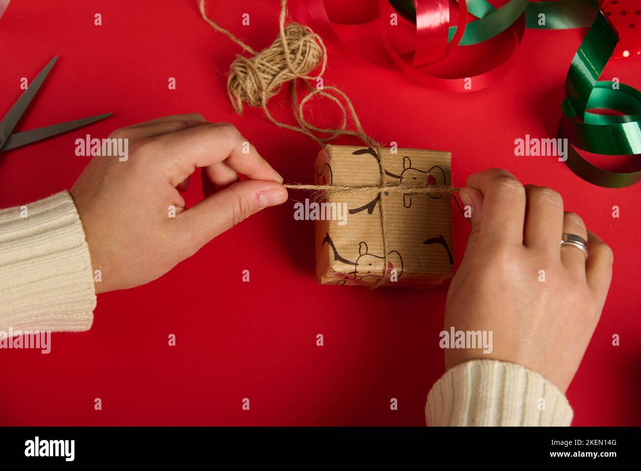 Top view of woman tying up a Christmas gift with a linen rope, over a ...