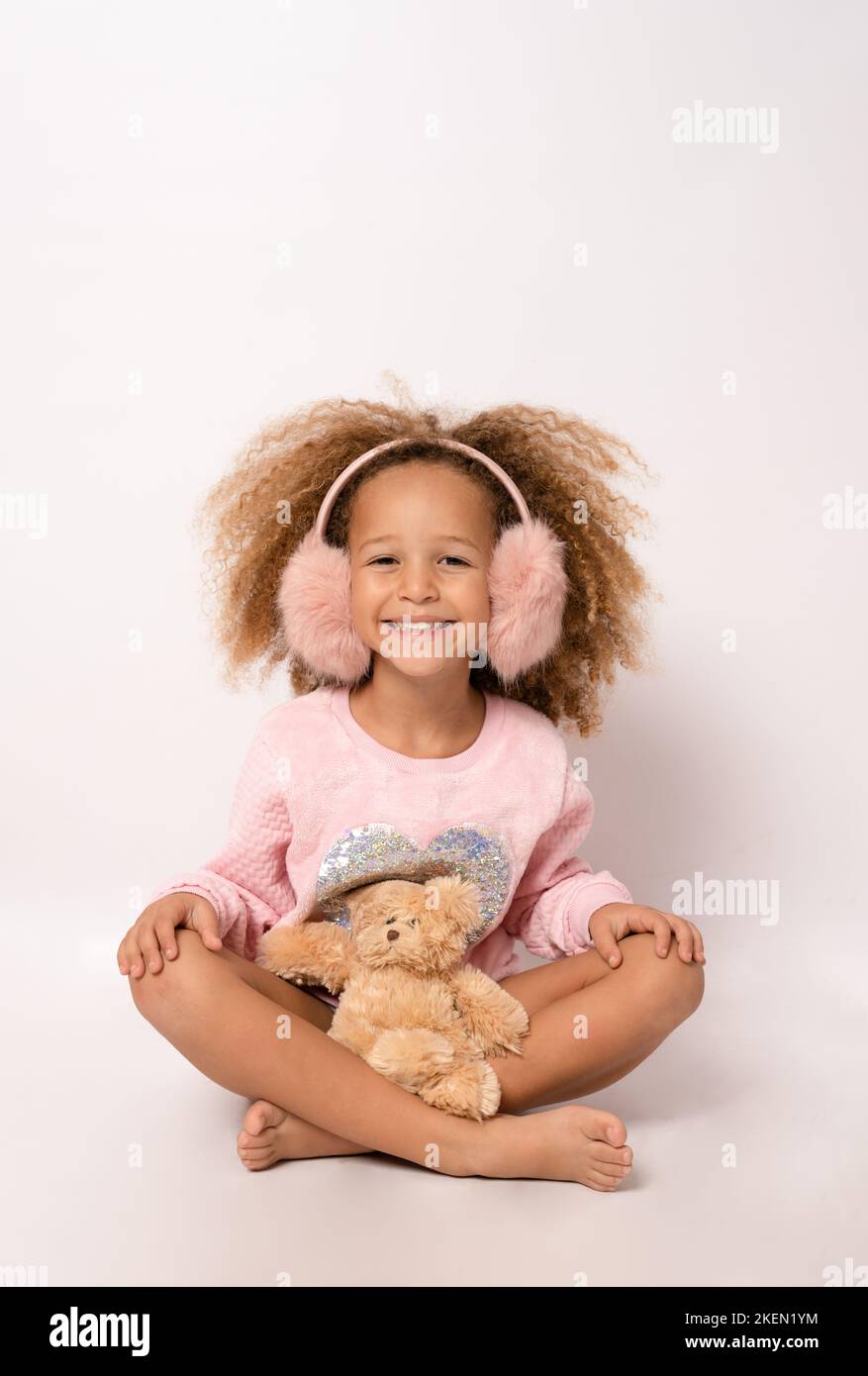 Little child girl wearing earmuffs is hugging teddy bear isolated over ...