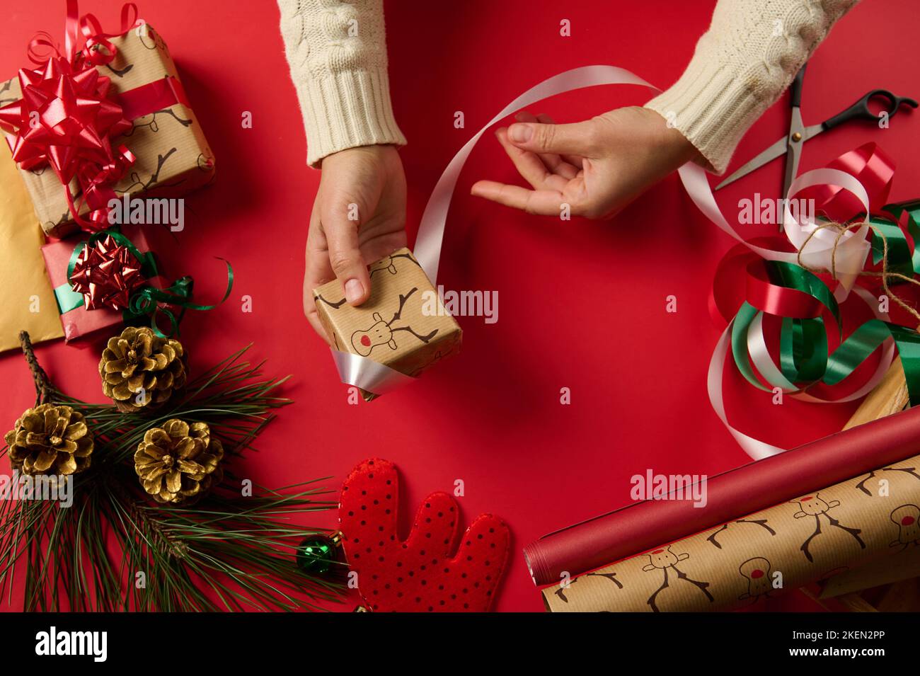 Directly above, woman's hands wrapping a small present in a gift paper ...