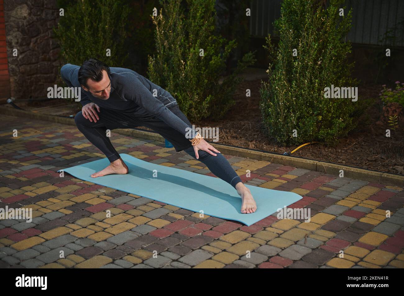 Full length. Man athlete, standing barefoot on a yoga mat, stretching ...