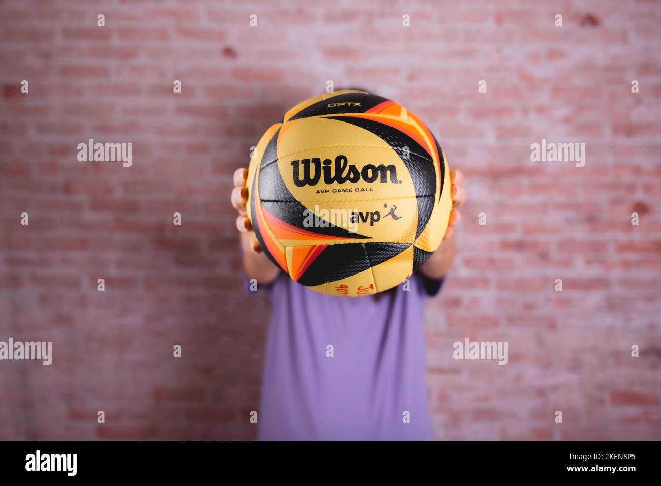 A person holding a Wilson volleyball in front of him on a brick wall ...