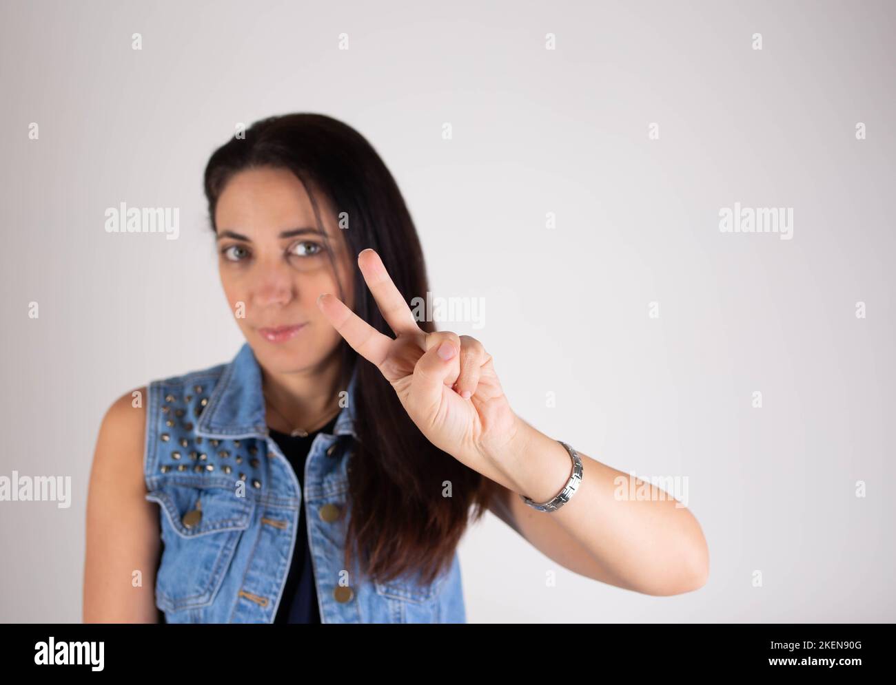 A beautiful brunette in a denim jacket shows a peace sign with her ...