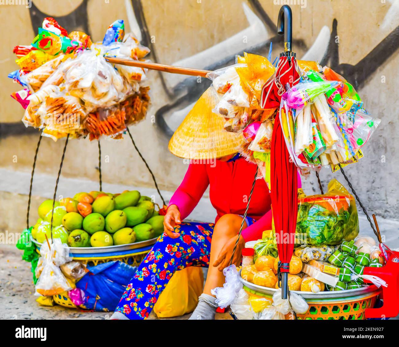 A man in a clown costume on the street sells colorful goods and fruits ...