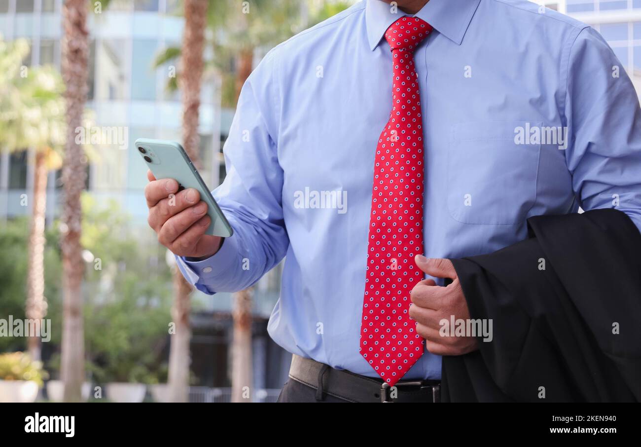 A businessman in a jacket with a red tie holding a phone in his hand ...