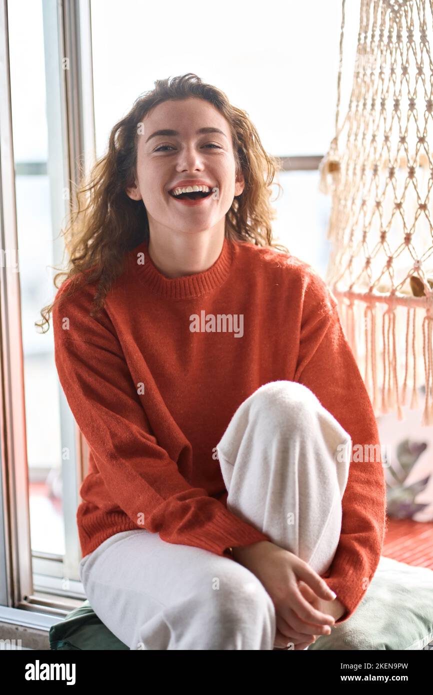 Happy pretty young woman sitting on windowsill at home and laughing ...