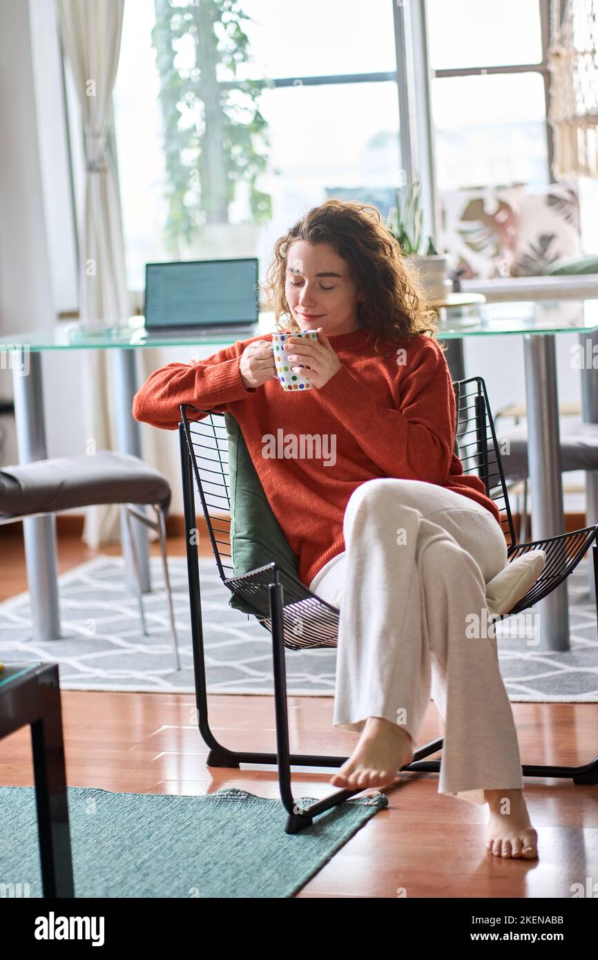 Young happy pretty woman sitting on chair drinking tea coffee at home ...