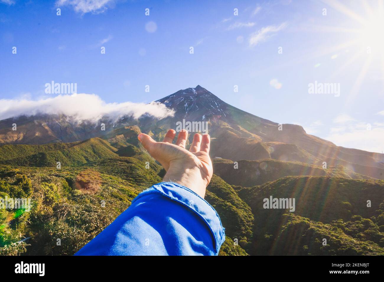 A person's hand pointing at the beautiful evergreen Mount Taranaki in ...