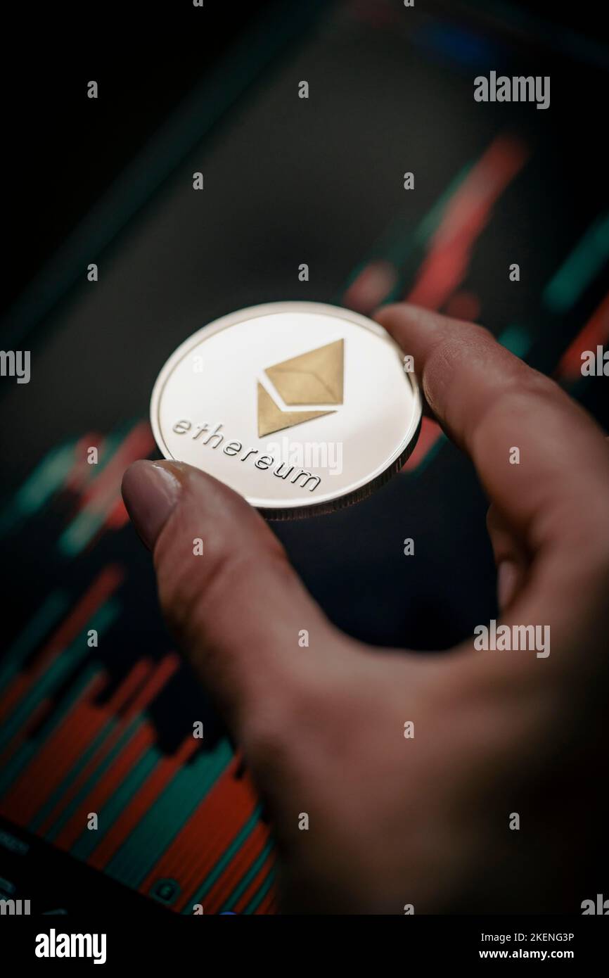 Hand holding a silver Ethereum (ETH) cryptocurrency coin with candle ...