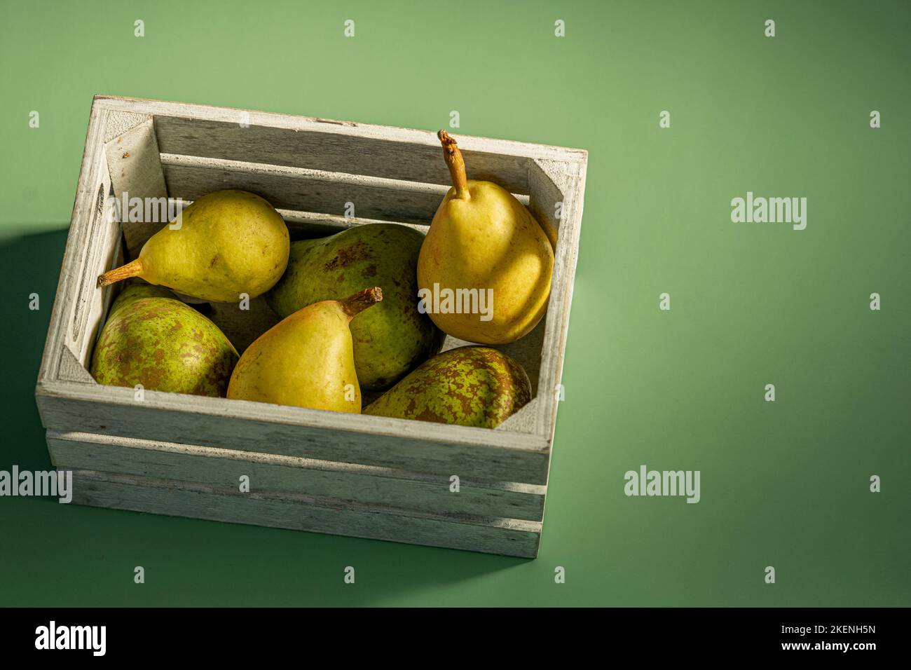 Wooden box full of ripe pears of different varieties on plain green ...