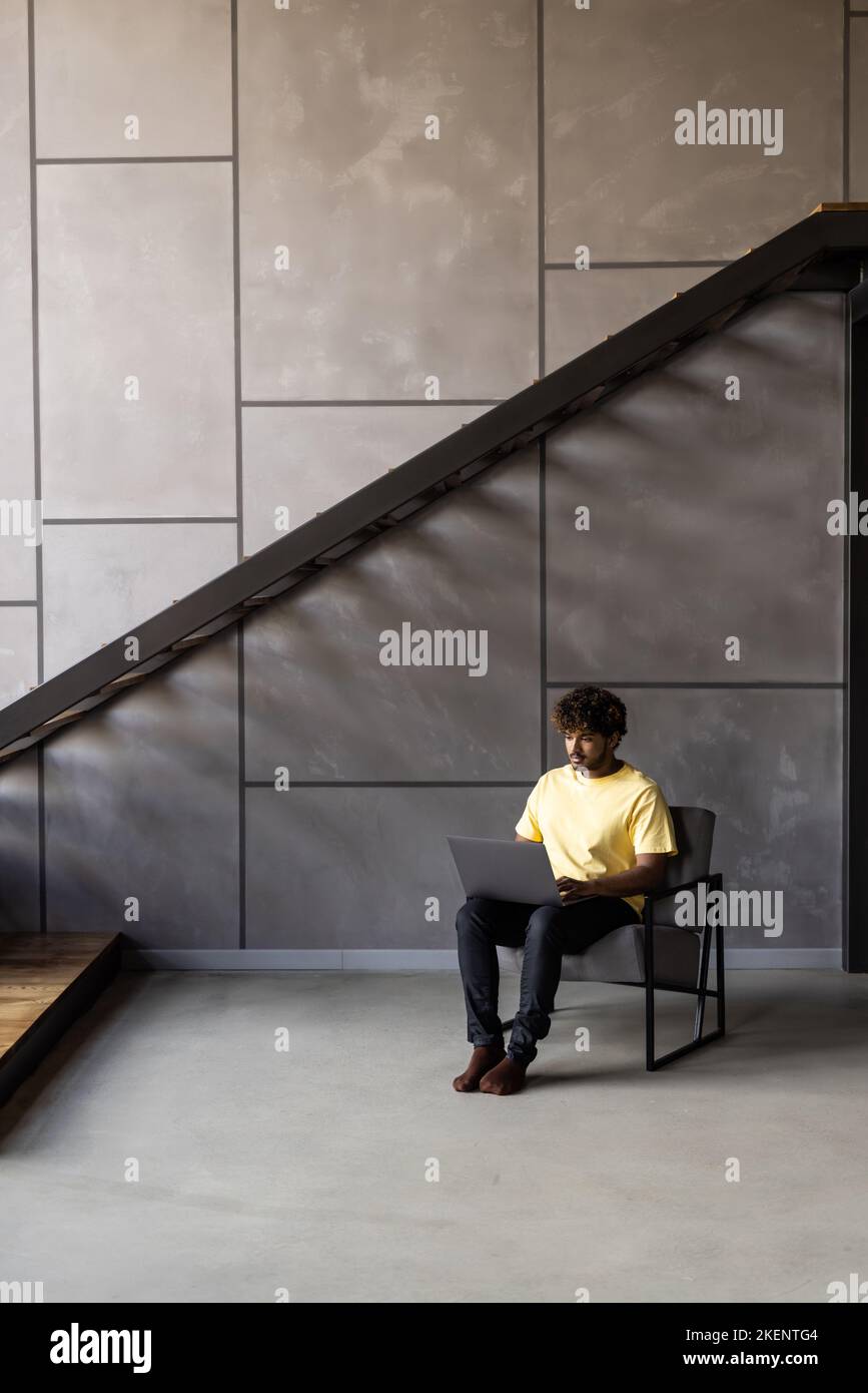 Handsome man working on laptop and smiling while sitting in big ...