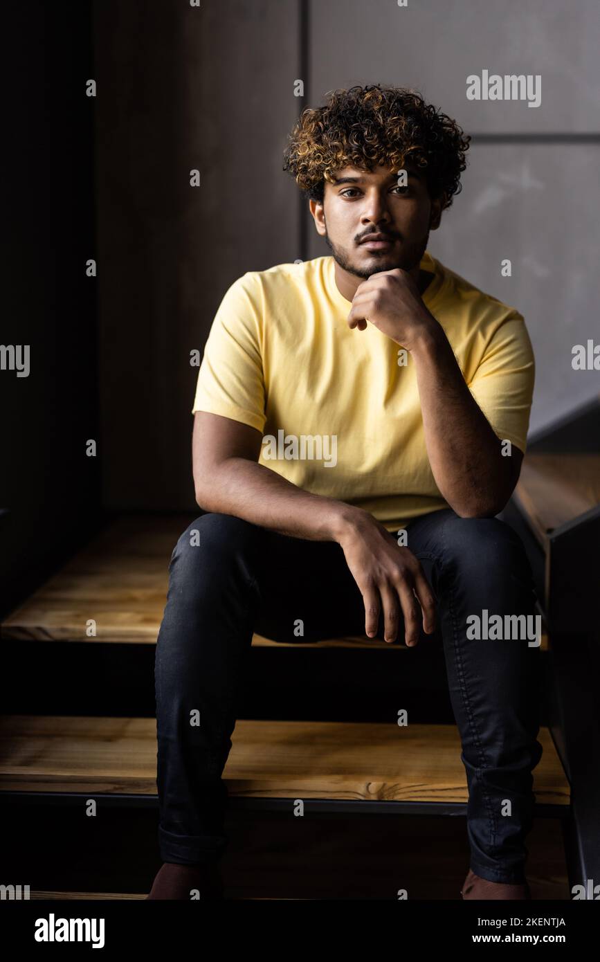 Thoughtful indian man user sitting at home on stairs relaxing wearing ...