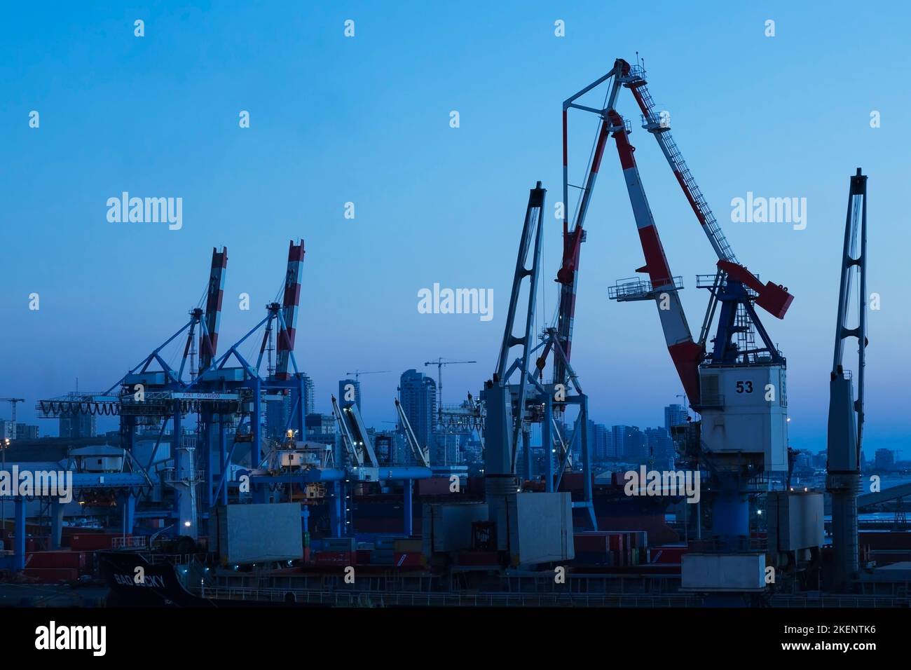 Silhouetted four-link cargo loading crane and docked cargo ship ...