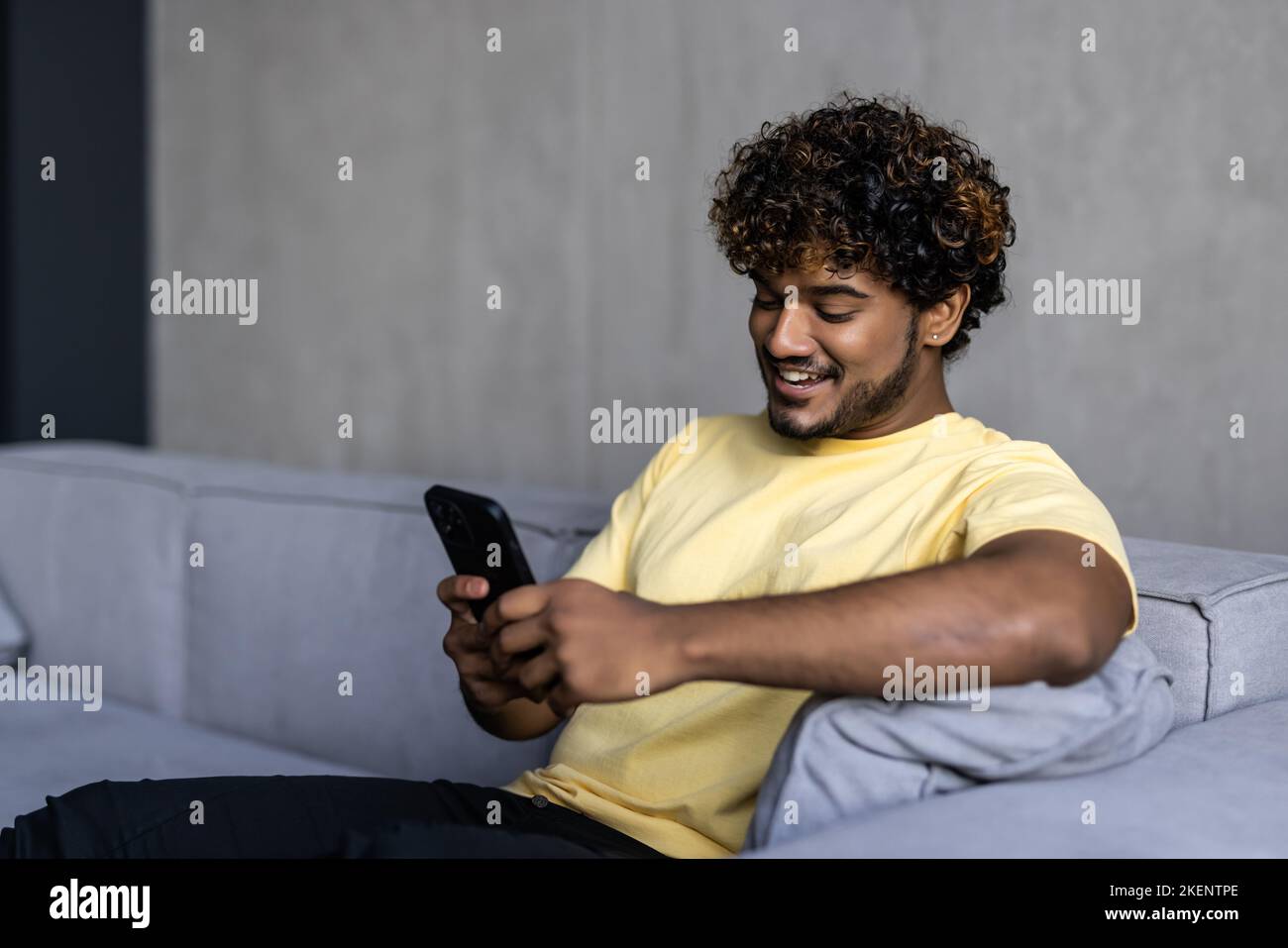 Young indian boring man with headphones on his neck holding phone and ...