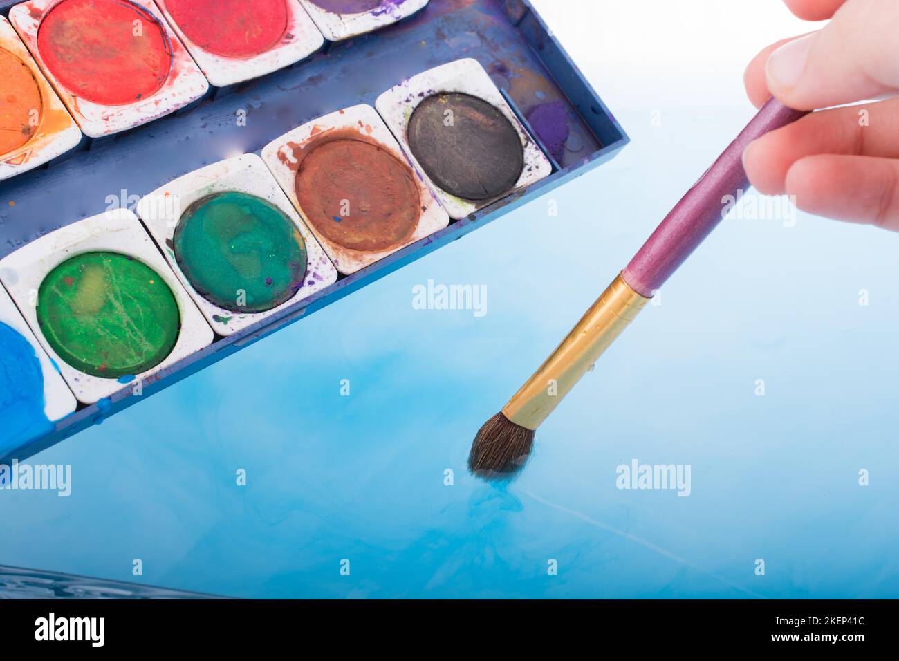 Watercolor paint dissolving in water as painting brush touches water ...