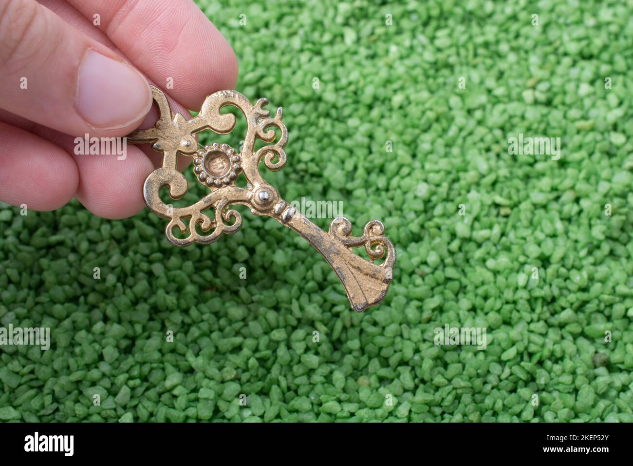 Hand holding retro style gold color key on green sand Stock Photo - Alamy