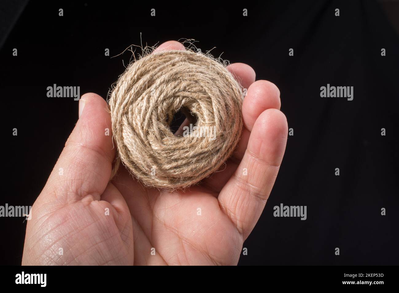 Spool of brown string in hand on black background Stock Photo - Alamy