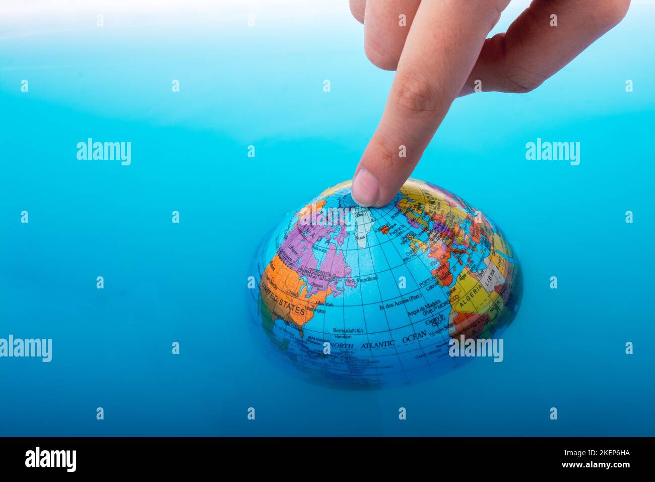 Little globe with finger on top floating in blue water Stock Photo - Alamy