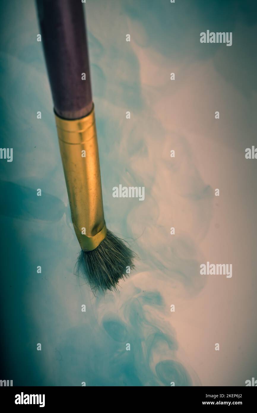 Watercolor paint dissolving in water as painting brush touches water ...