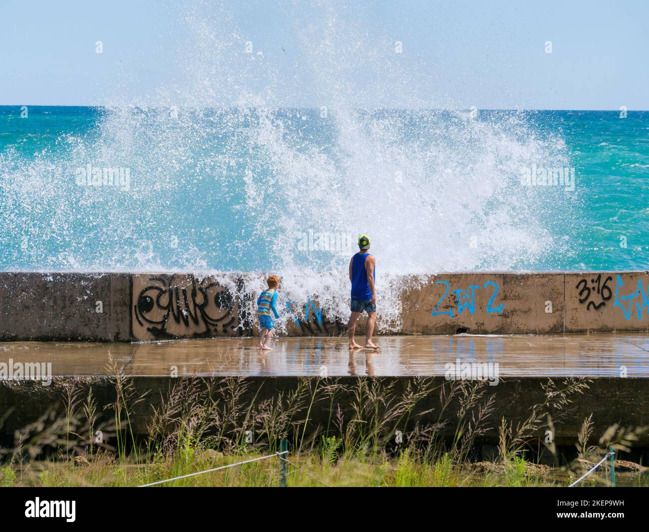 A father and his young son brave the seawall as a large wave crashes ...