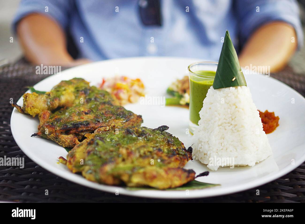 A plate of spiced herbal karee roasted duck with a rice cone, sambal ...