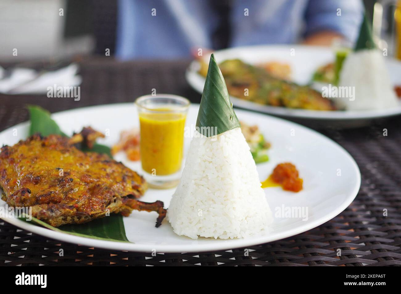 A plate of spiced herbal karee roasted duck with a rice cone, sambal ...