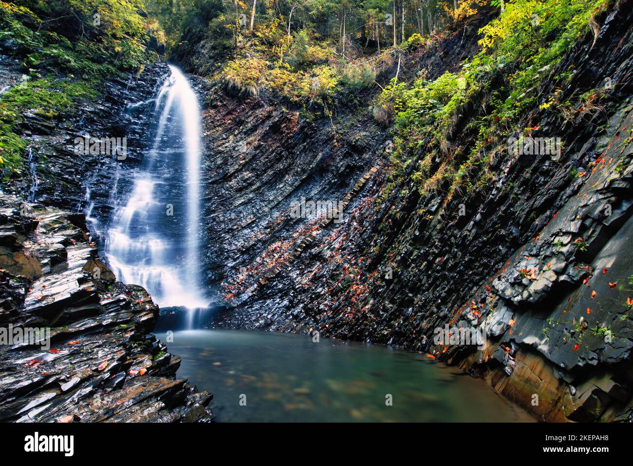 Mountain waterfall. Precipitous stone rock, grass and trees. A ...
