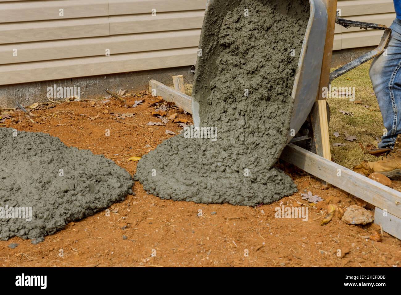 Construction worker pours cement from wheelbarrow to create concrete ...