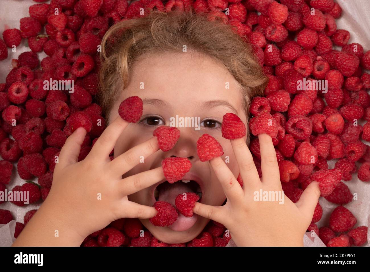 Funny kids face near raspberry background. Cute child eats raspberries ...
