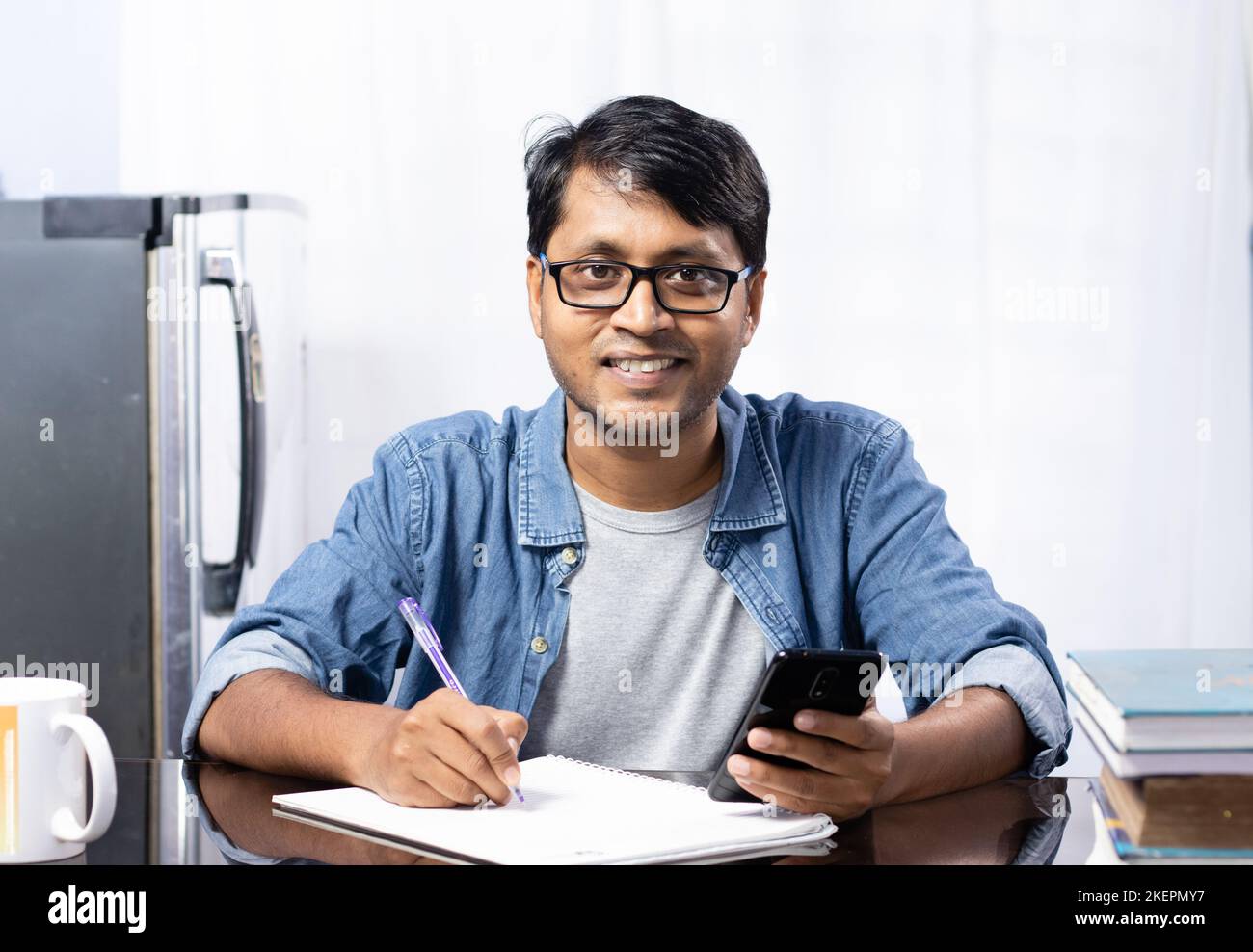 An Indian young male looking at camera with smiling face while studying ...