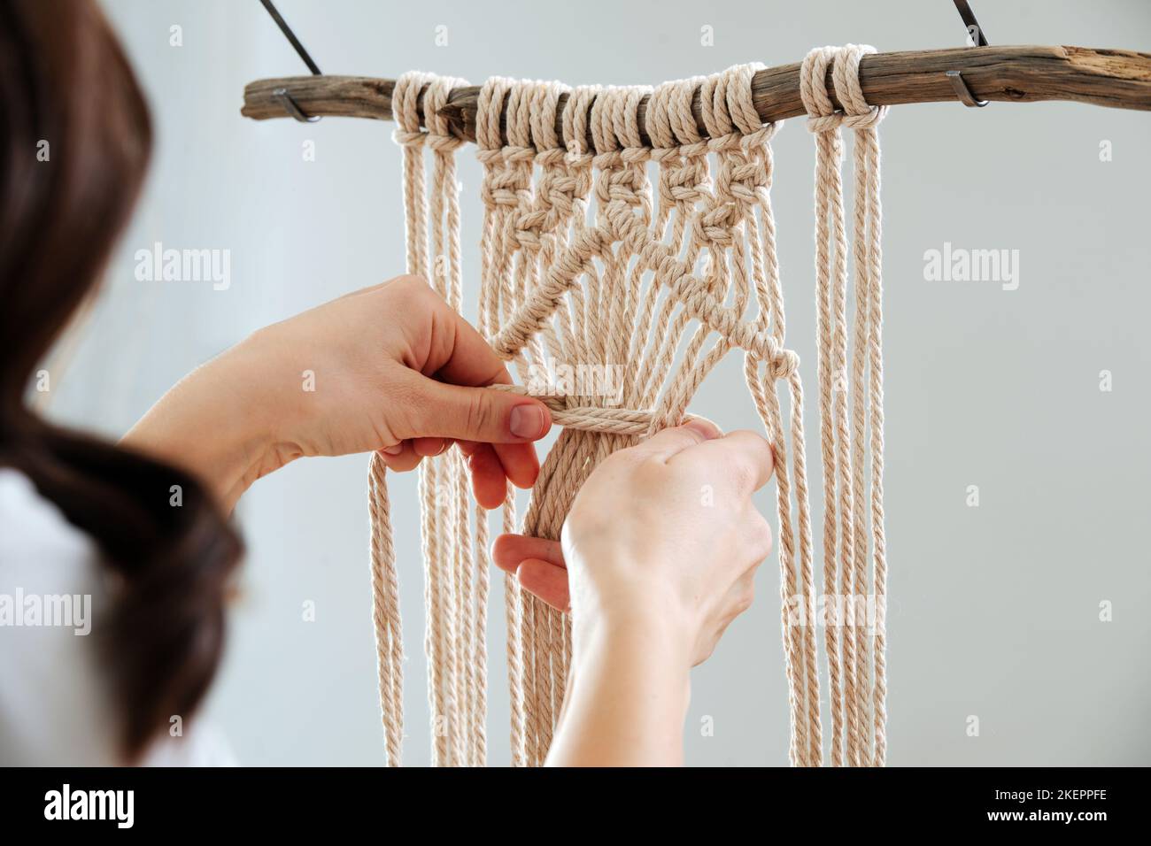 Woman working on a macrame piece suspended from a stick. IT's still in ...
