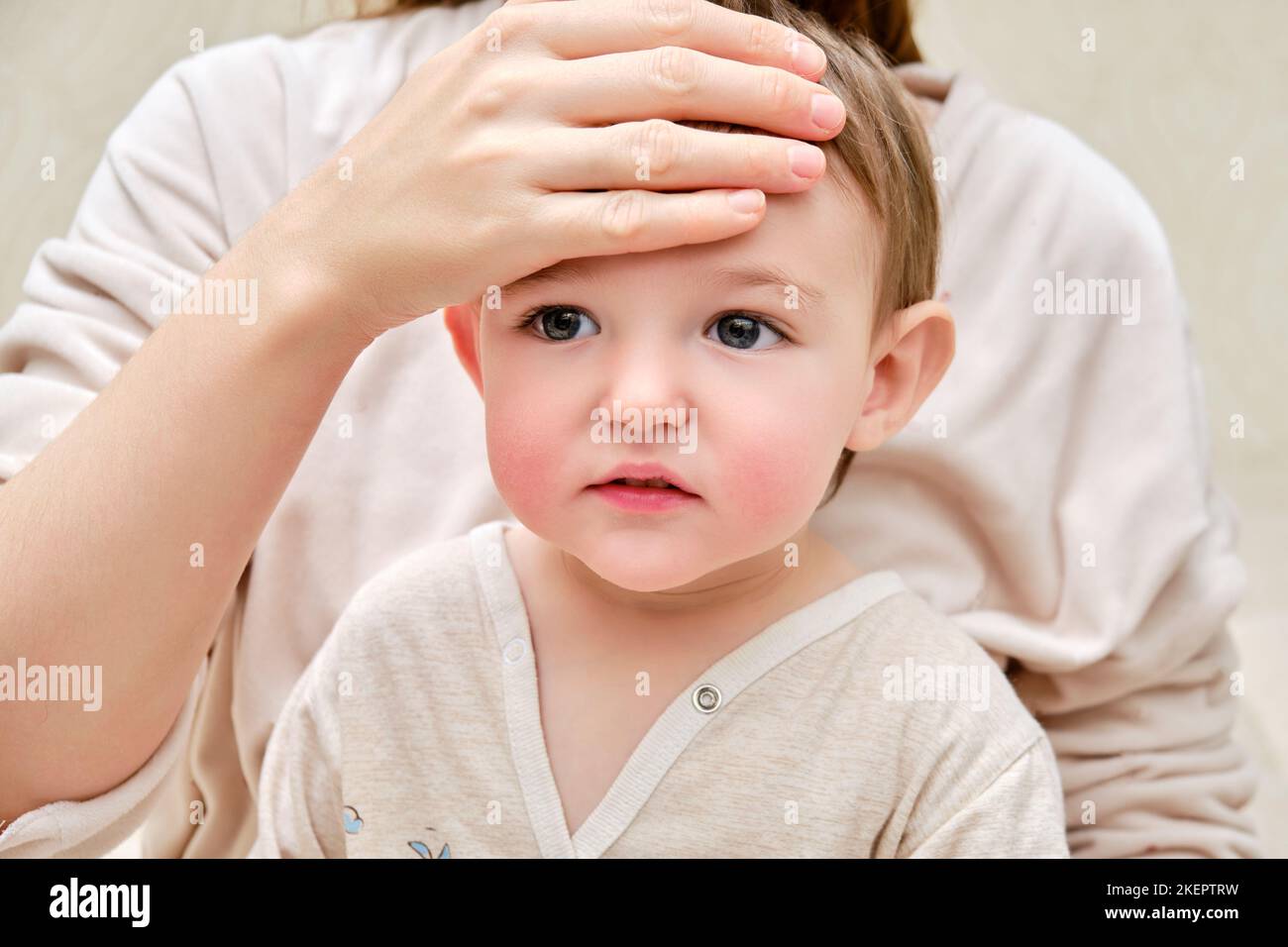A mother woman measures the temperature of a ill toddler baby with her hand. Mom checks the high ...