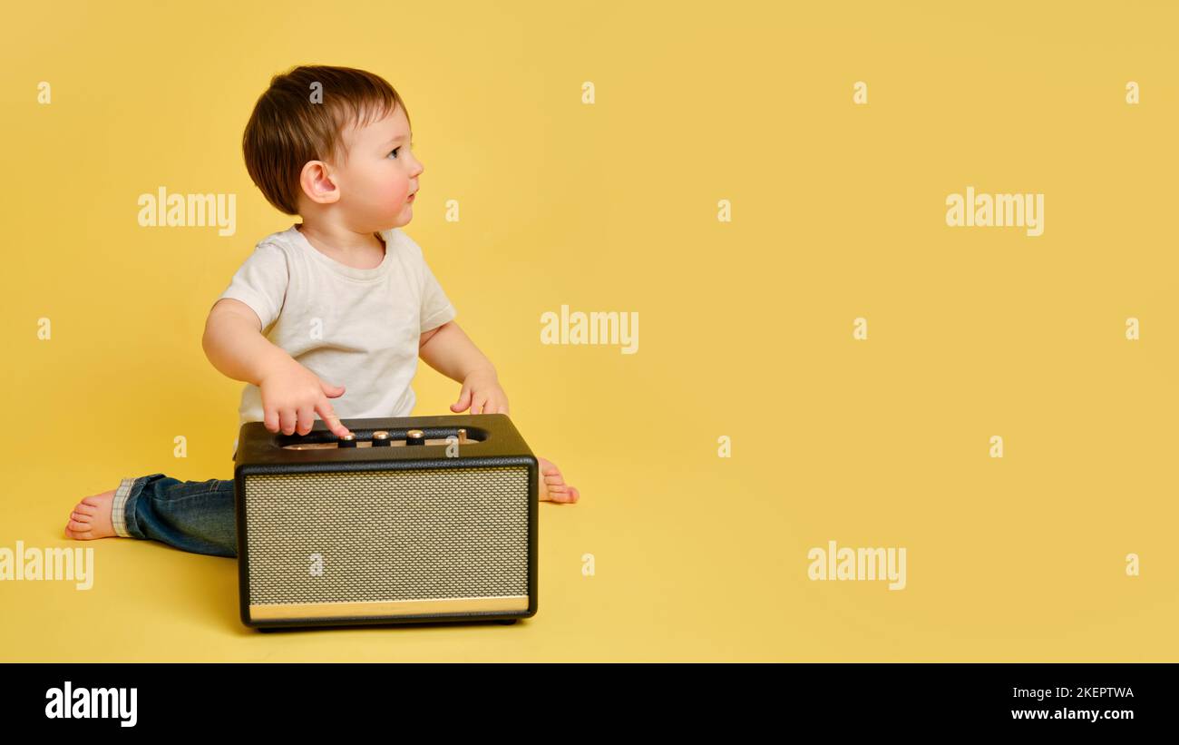 Toddler baby plays with a wireless music speaker on a studio yellow ...