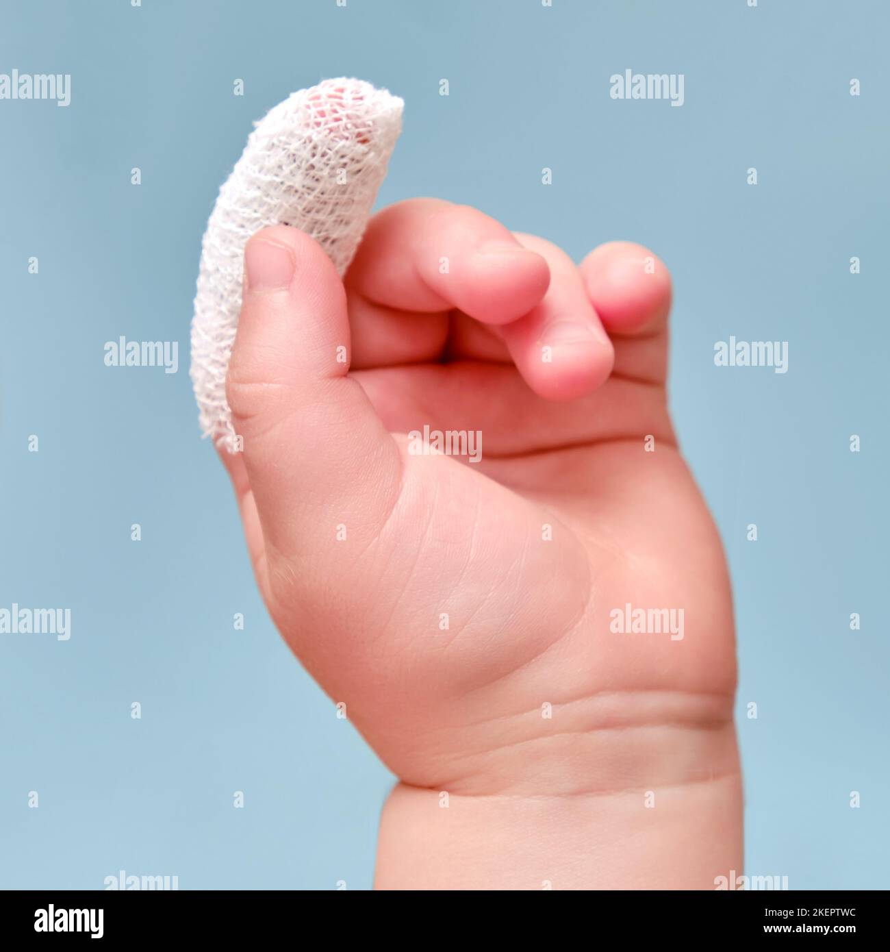 Baby s hand with a bandaged finger on a blue studio background, close ...