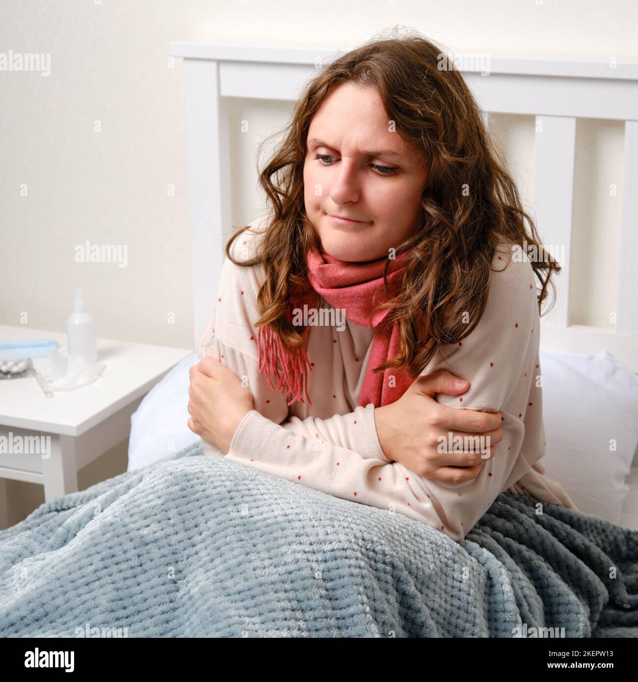 A woman is freezing from the cold sitting on a home bed, fever and high ...
