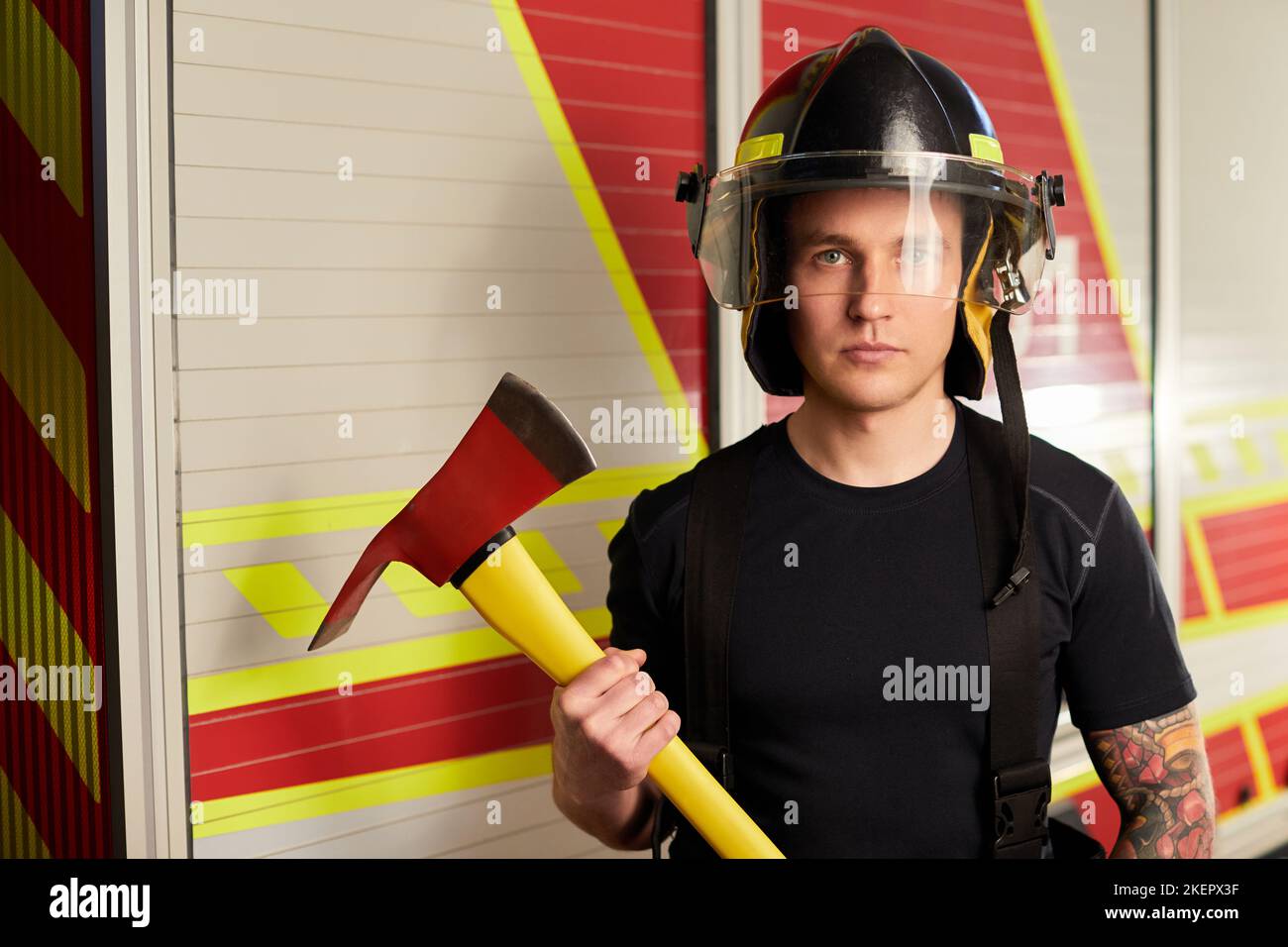 Photo of fireman wearing helmet with ax against fire engine Stock Photo ...