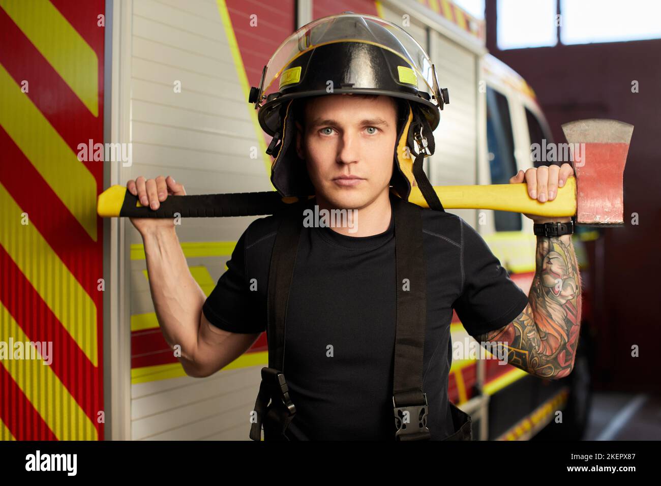 Photo of fireman wearing helmet with ax against fire engine Stock Photo ...