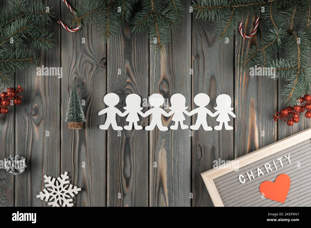 Group of paper cut people on gray wooden wall, top view. Helping needy ...