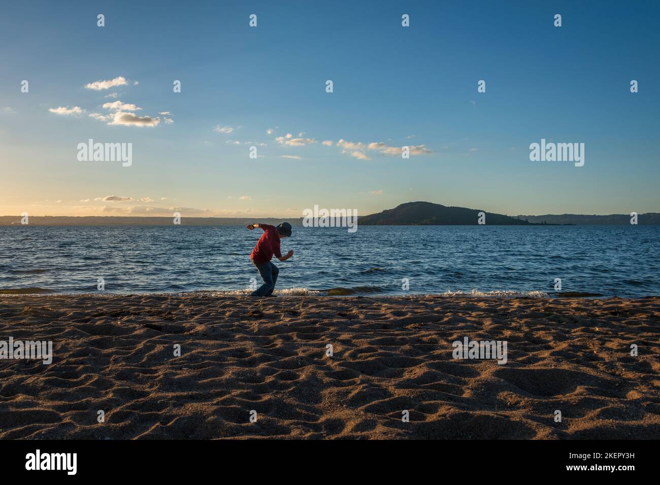 A tourist stone skipping at Lake Rotorua at sunset, Mokoia Island in ...
