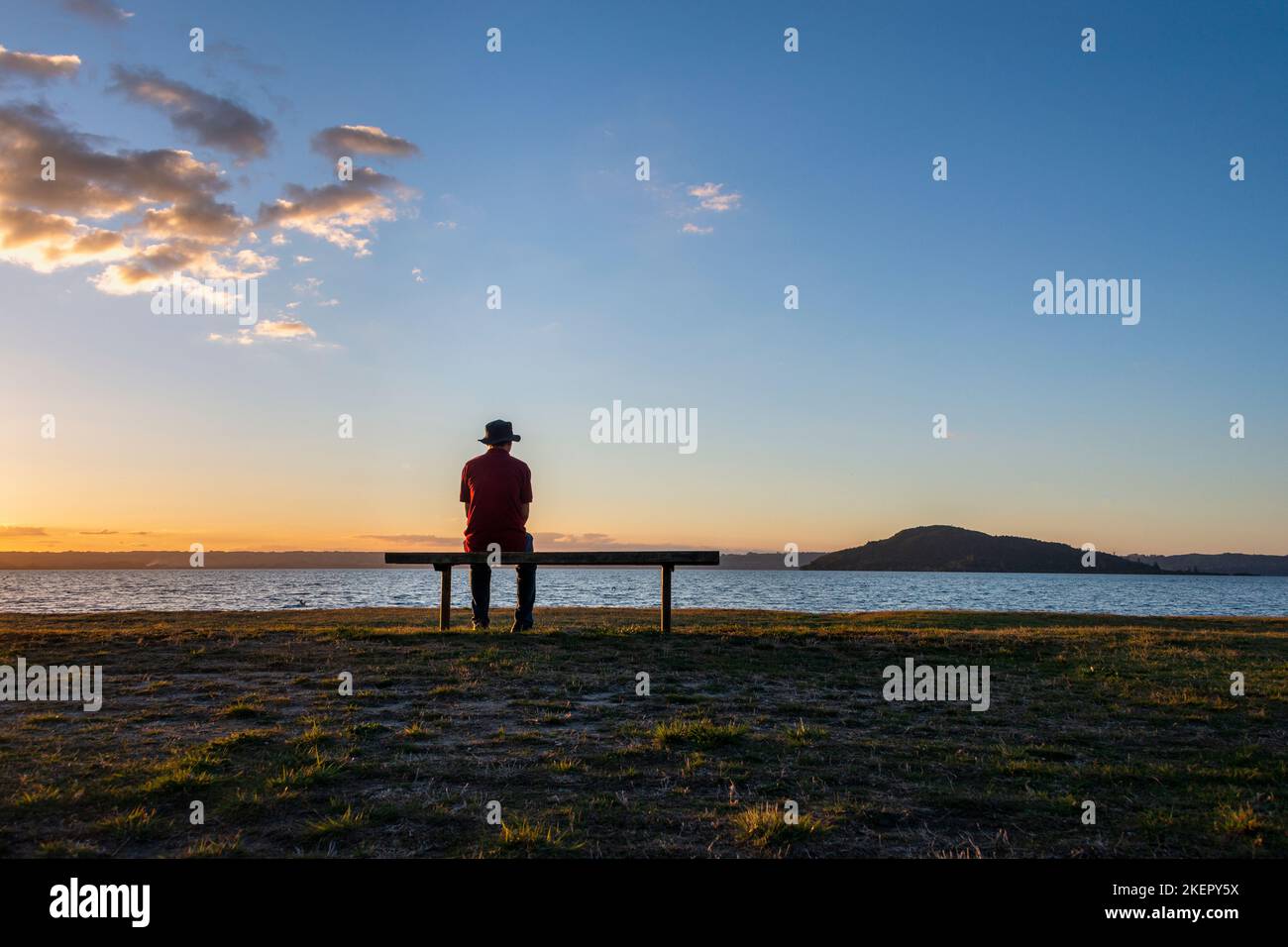 Man sitting alone by lake Rotorua at sunset, Mokoia Island in the ...