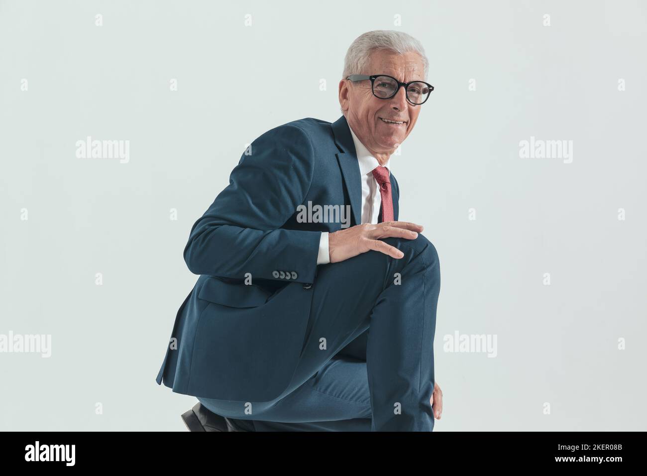 side view of happy old man crouching and touching knee with palms while ...