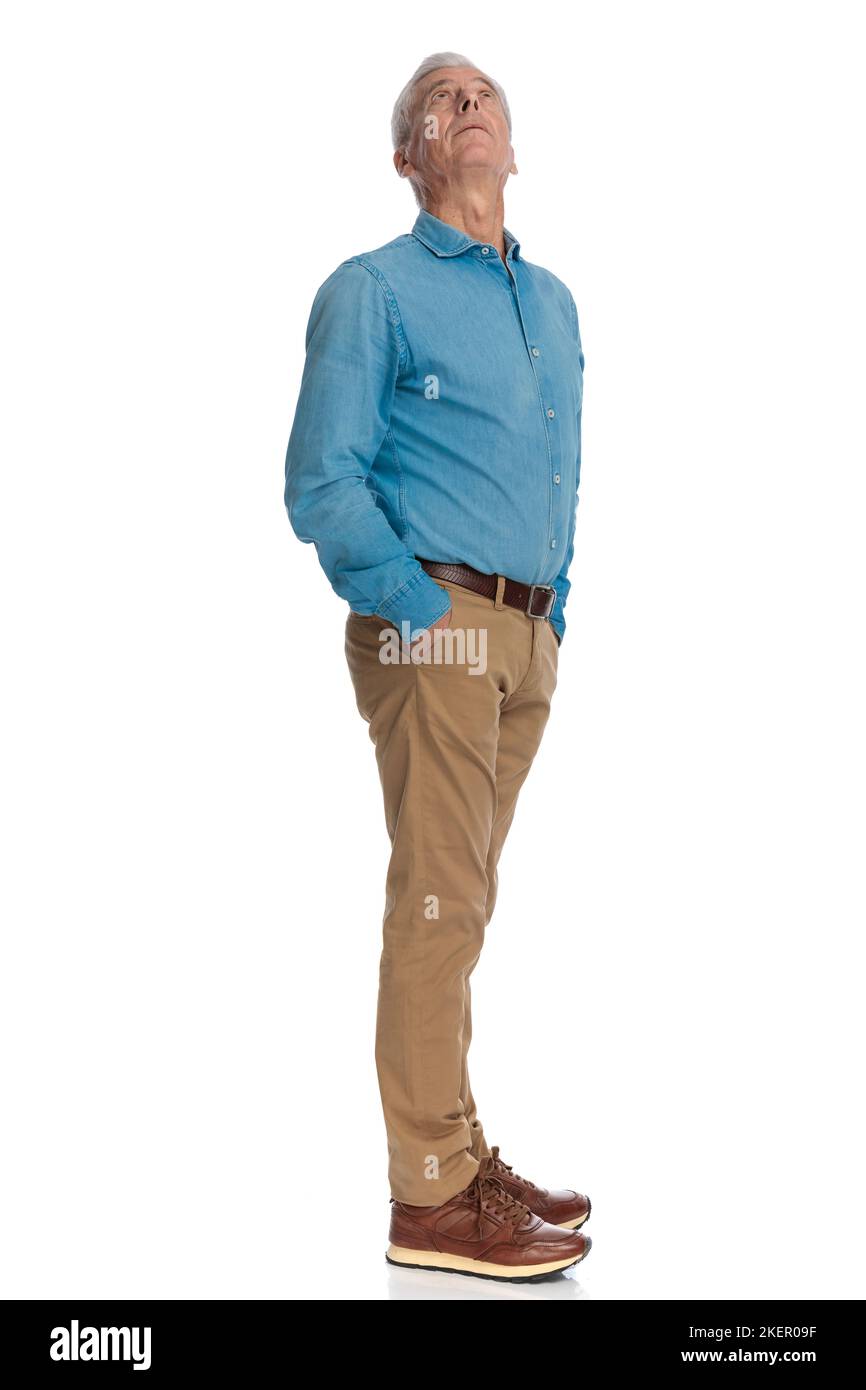 curious old man in his 60s holding hands in pockets and looking up ...