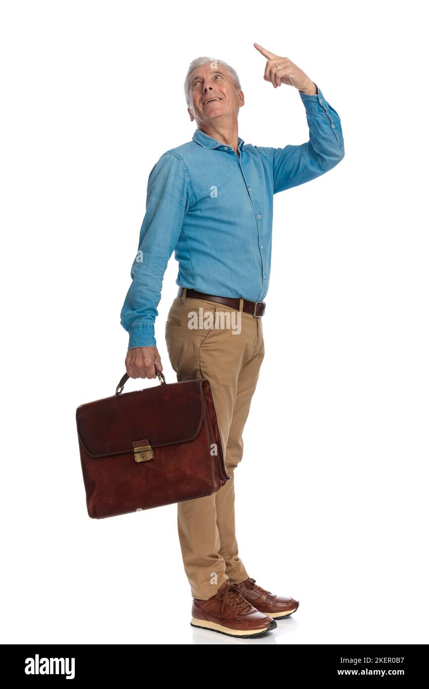 old man in his 60s with bag looking up and pointing finger in the air ...