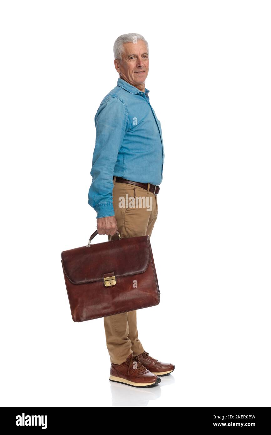 side view of casual old man in his 60s holding suitcase and standing in ...