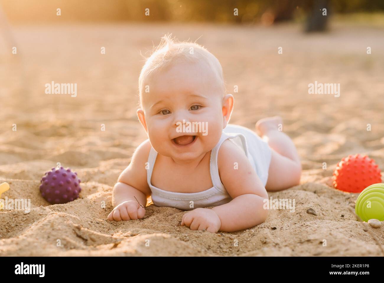 A happy little boy is lying on a sandy beach near the sea in the rays ...