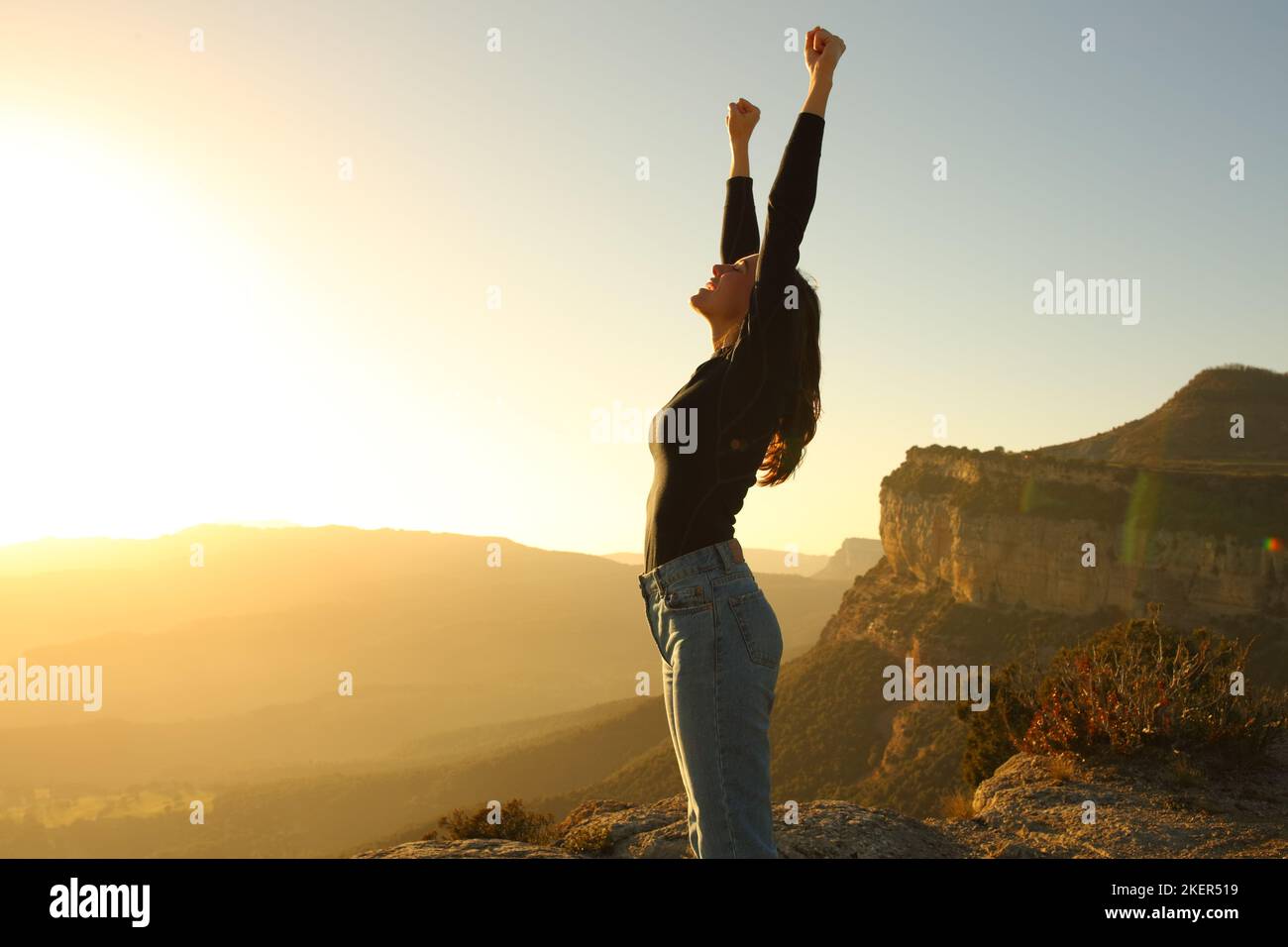 Side view portrait of an euphoric woman raising arms in the mountain at ...