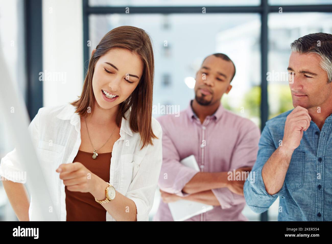 Sharing her ideas. three businesspeople working at a whiteboard Stock ...