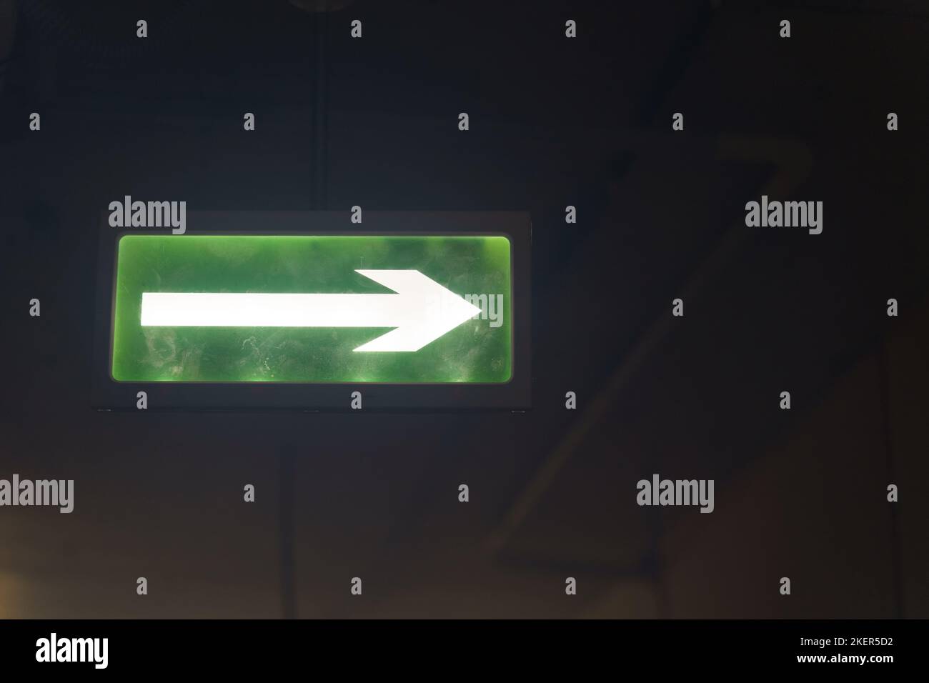 Illuminated green exit sign suspended from the ceiling in a public ...