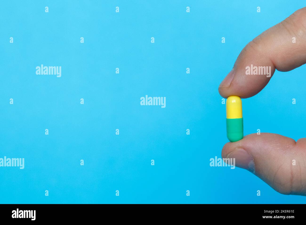 Male hand holds a pill. Isolated on a blue background. Pharmaceutical ...