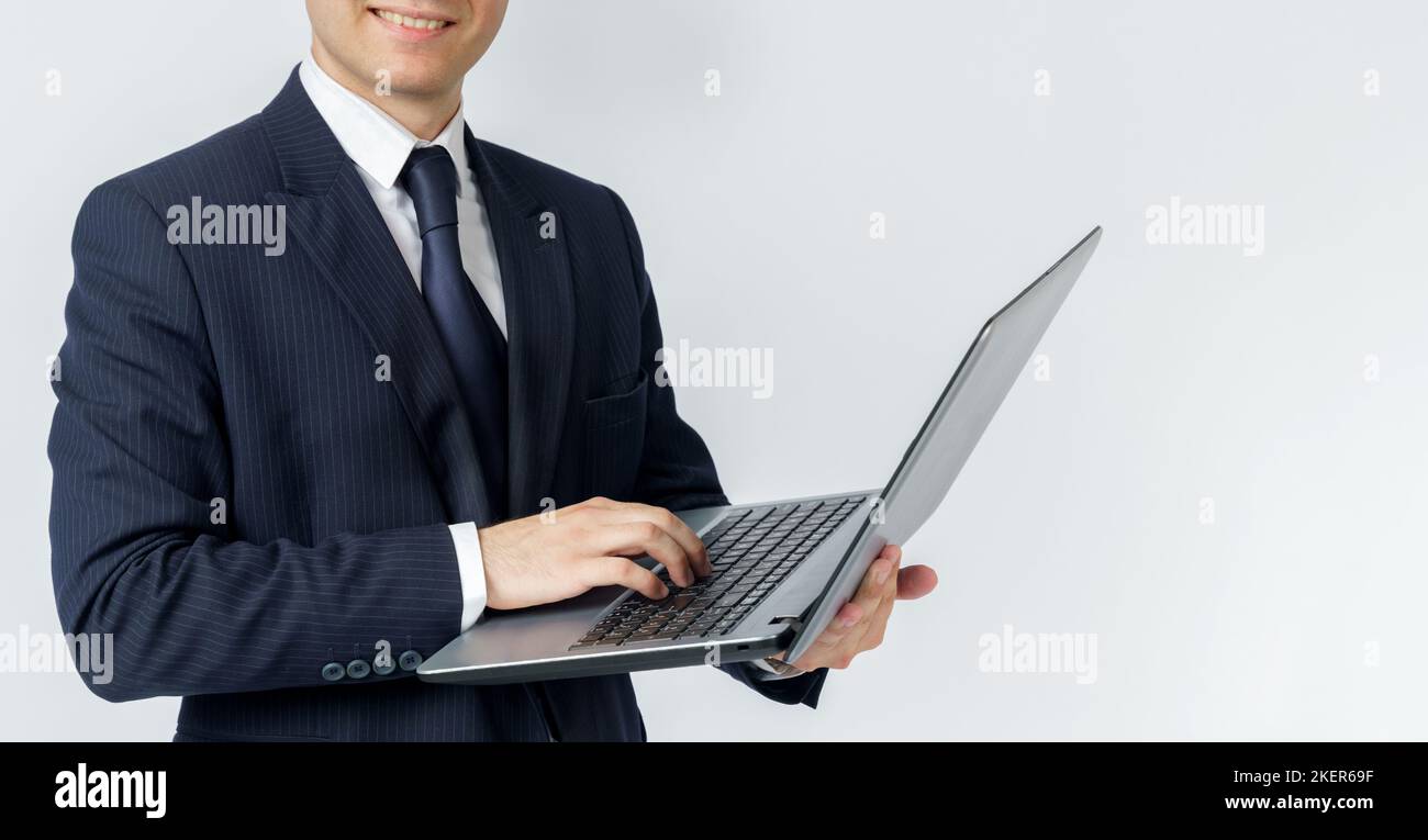 A businessman is holding a laptop in his hands, is typing with one hand ...