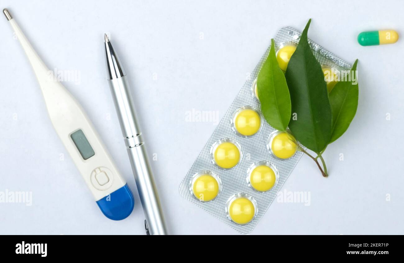 Yellow pills, thermometer and pen on a white background. Cold and flu ...